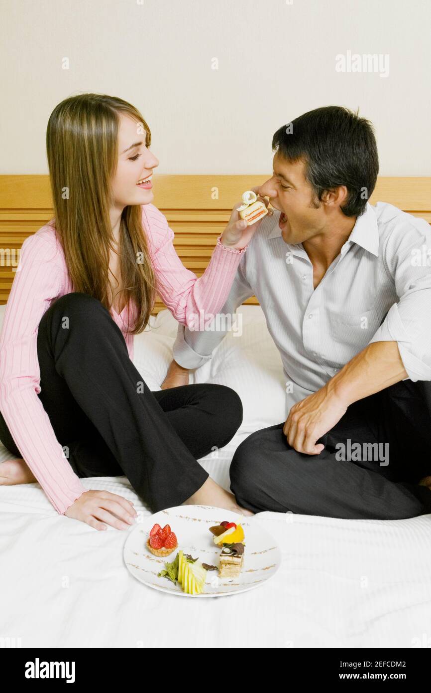 Young woman feeding cake to a mid adult man Stock Photo - Alamy