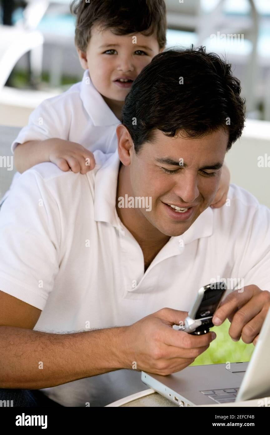 Close-up of a father using a mobile phone with his son standing behind ...