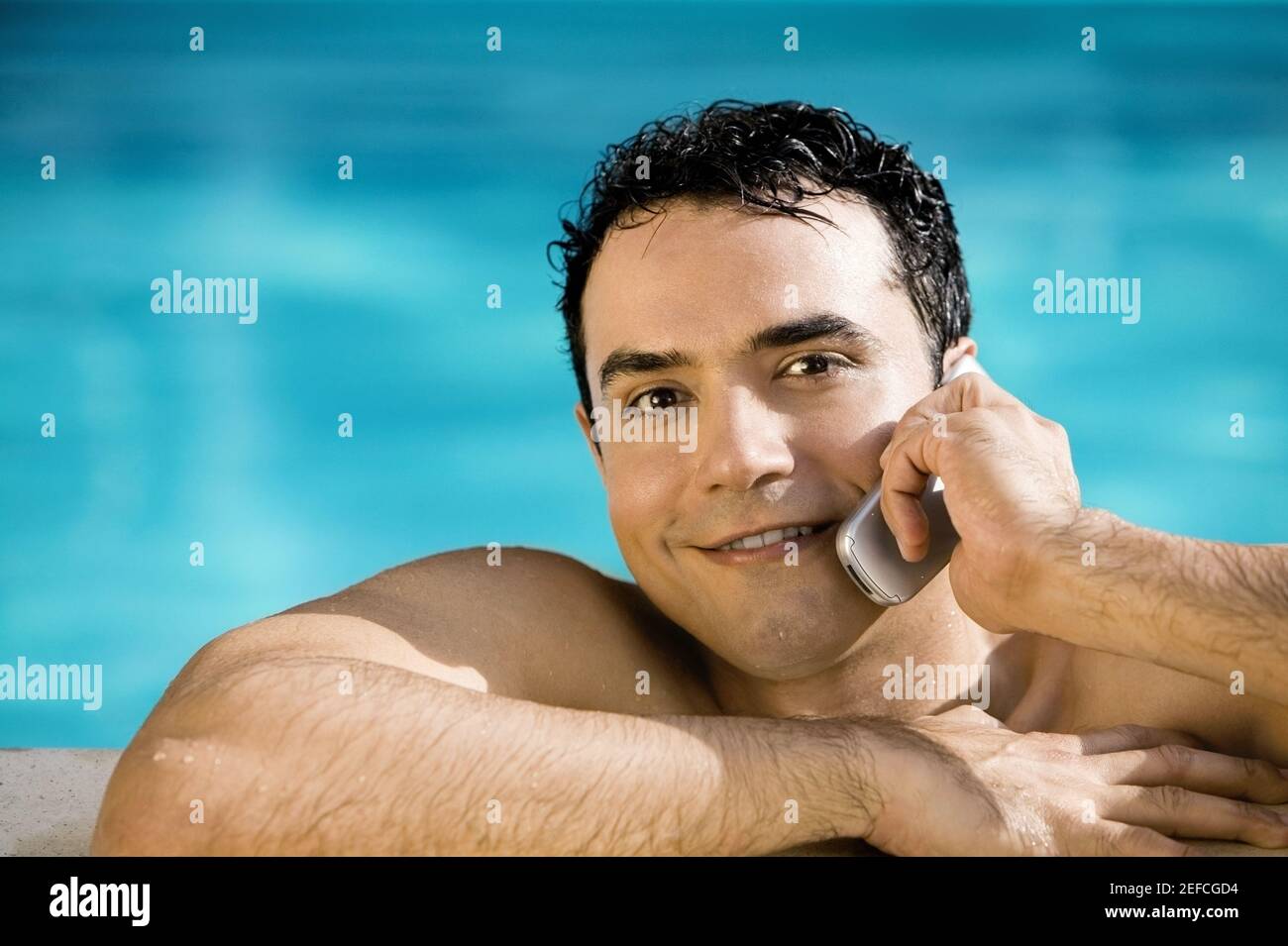 Portrait of a young man talking on a mobile phone in a swimming pool ...