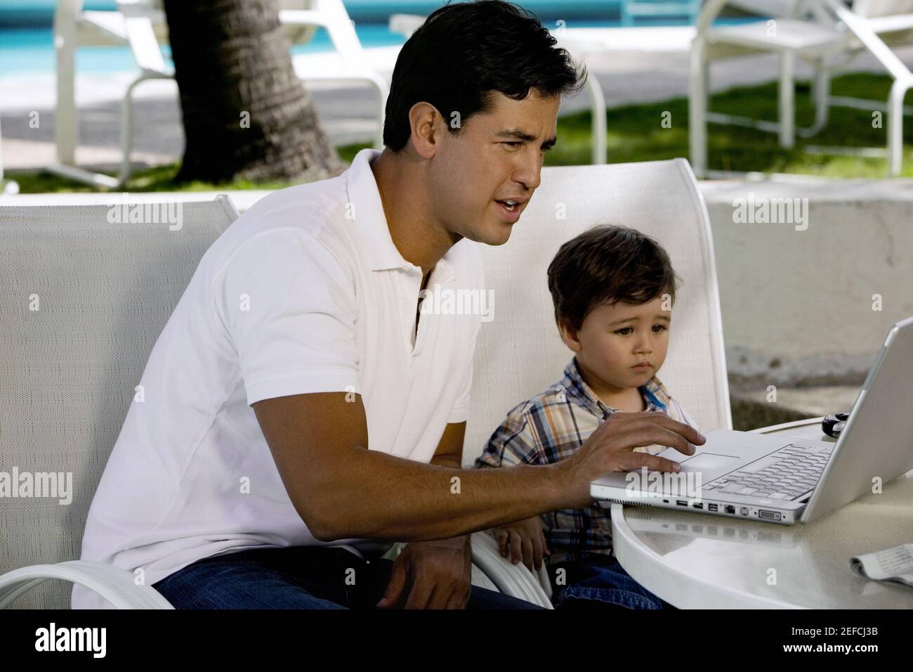 Side profile of a father working on a laptop with his son Stock Photo ...