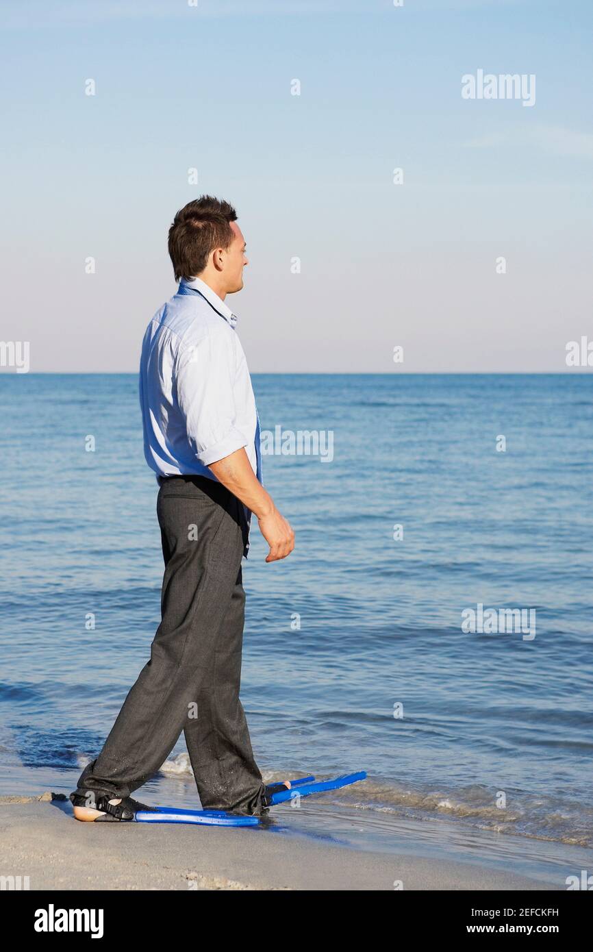 Side profile of a young man wearing flippers and walking on the beach ...