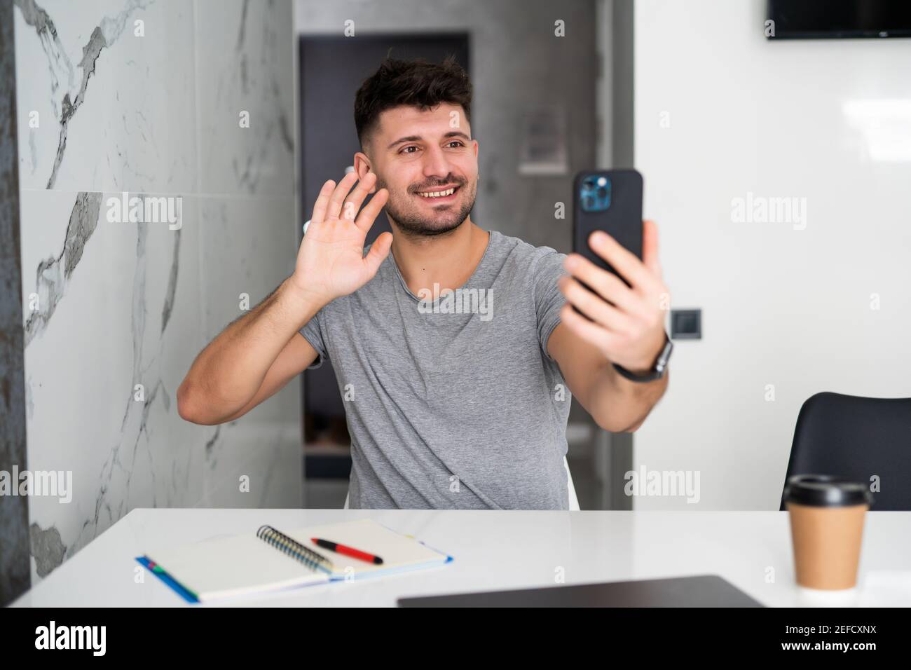 Young man having video call via smartphone in the home office ...
