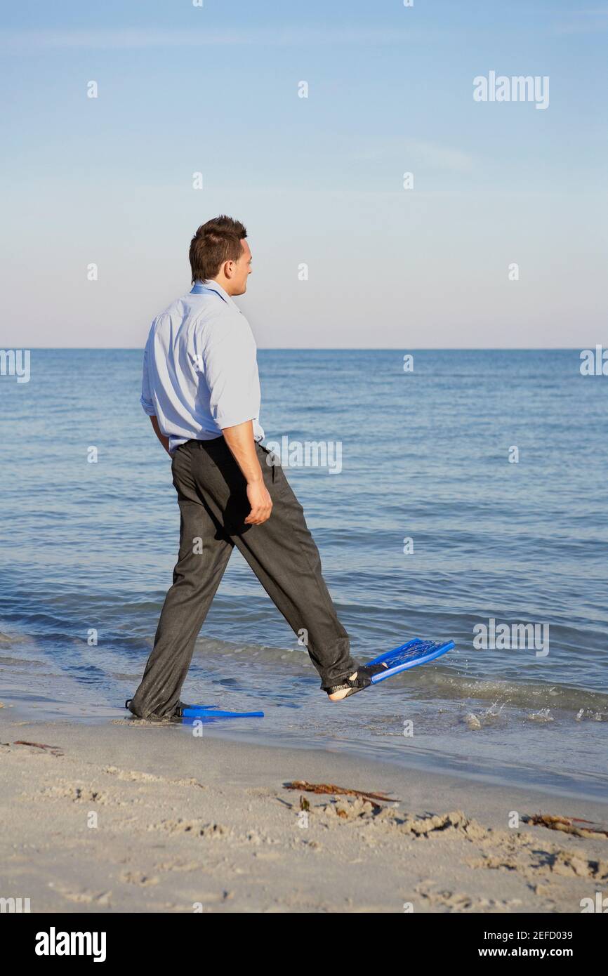 Side profile of a young man wearing flippers and walking on the beach ...