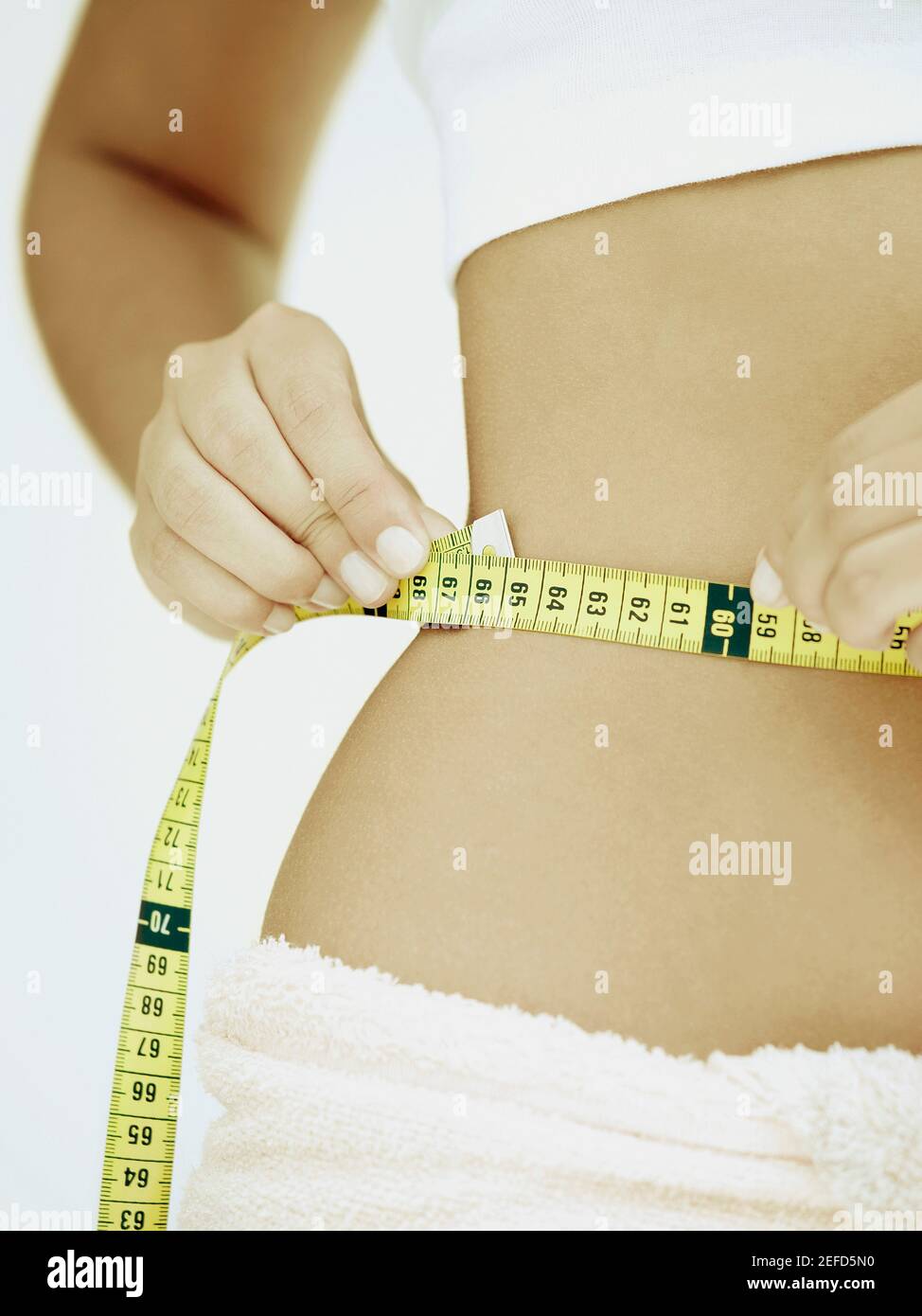 Mid section view of a woman measuring her waist with a tape measure ...