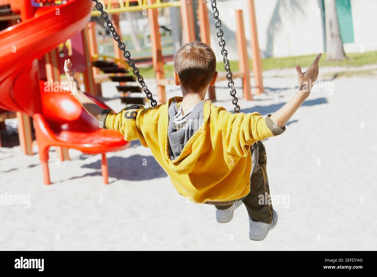 Rear view of a boy swinging on a chain swing ride with his arm ...