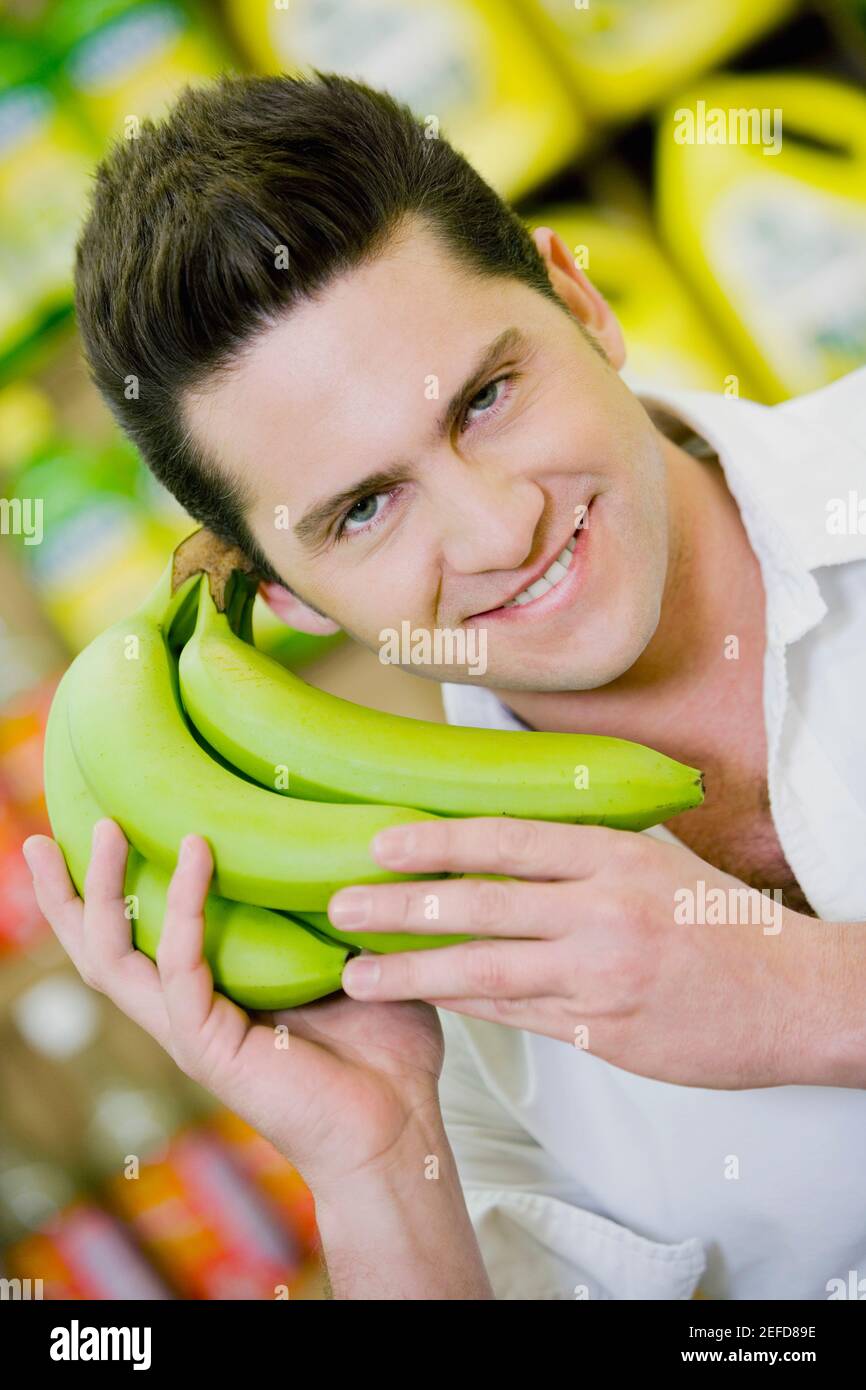 Portrait of a young man holding a bunch of bananas in a supermarket ...