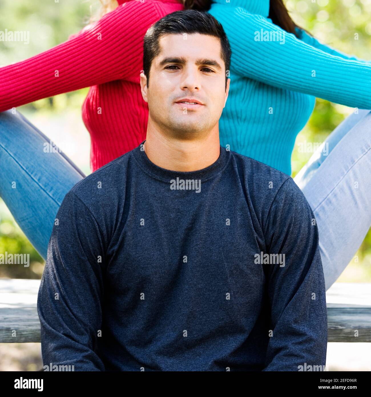 Portrait of a young man with two women sitting back to back behind him ...