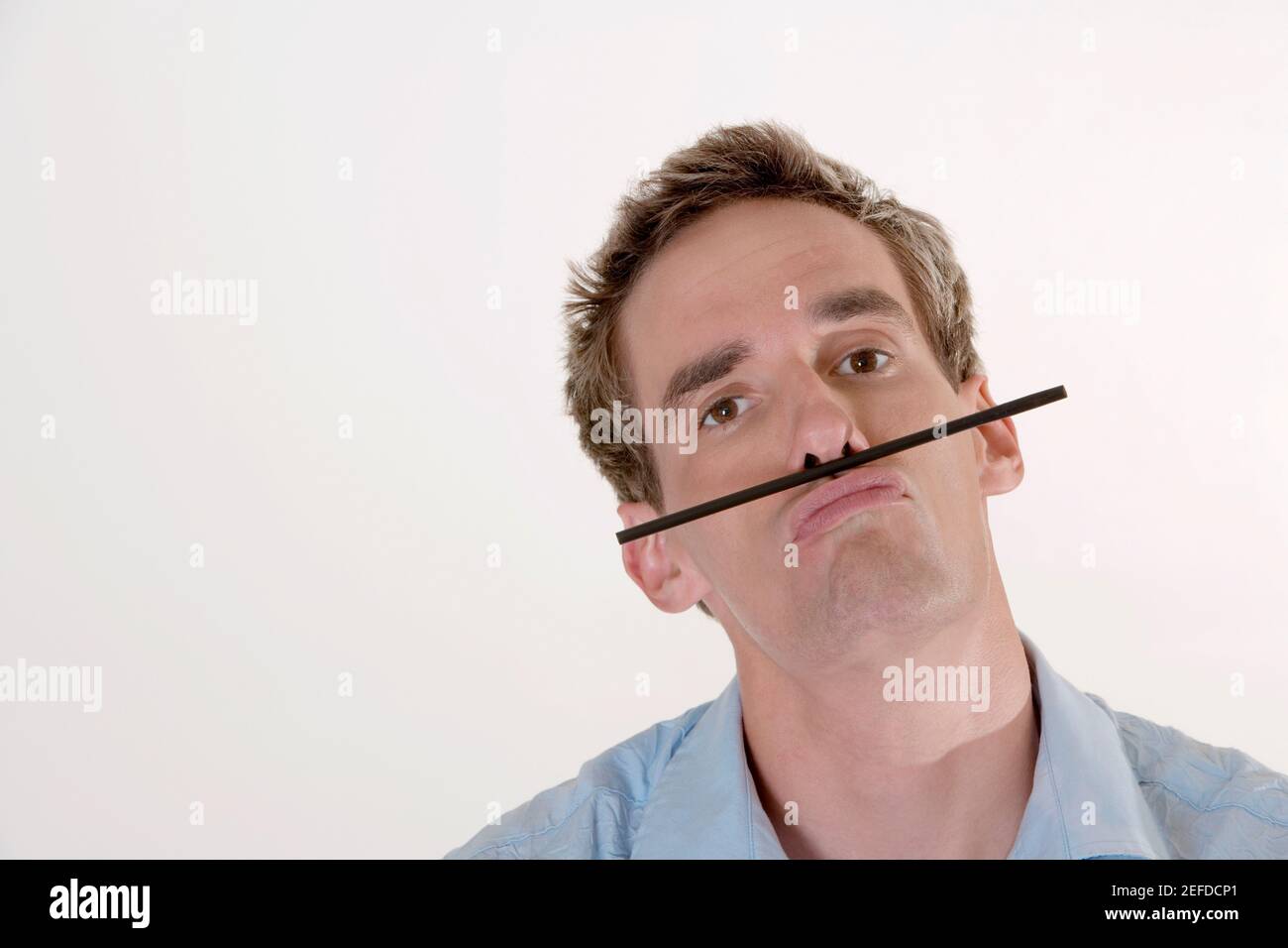 Portrait of a mid adult man balancing a drinking straw above his lips ...