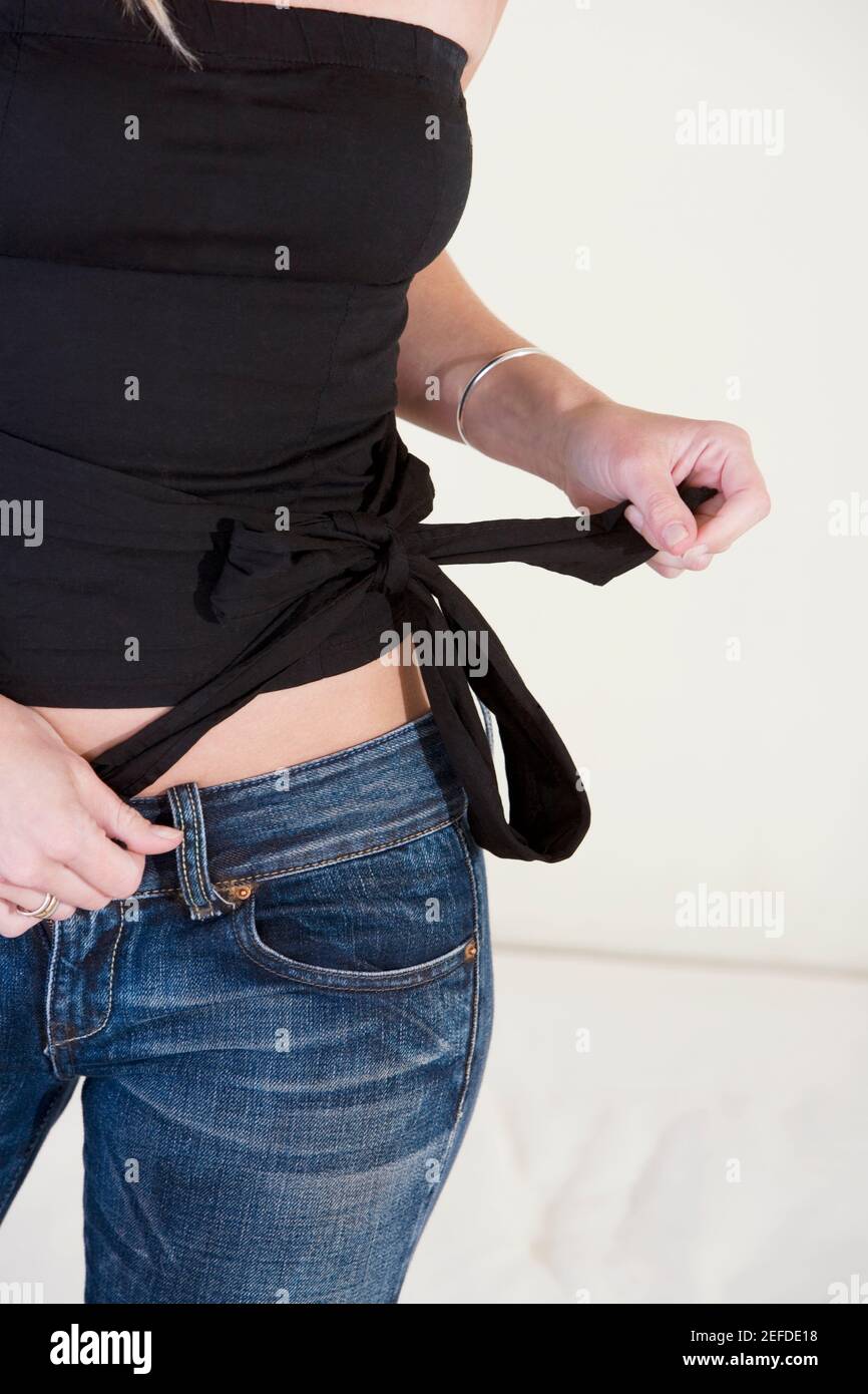 Mid section view of a young woman tying a knot on her top Stock Photo ...
