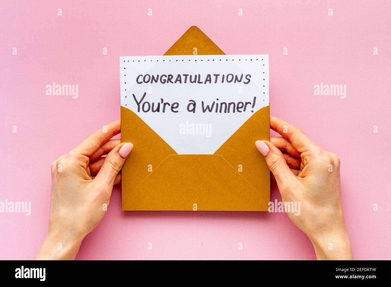 Hands holding award congratulation card in golden envelope. Text You're ...