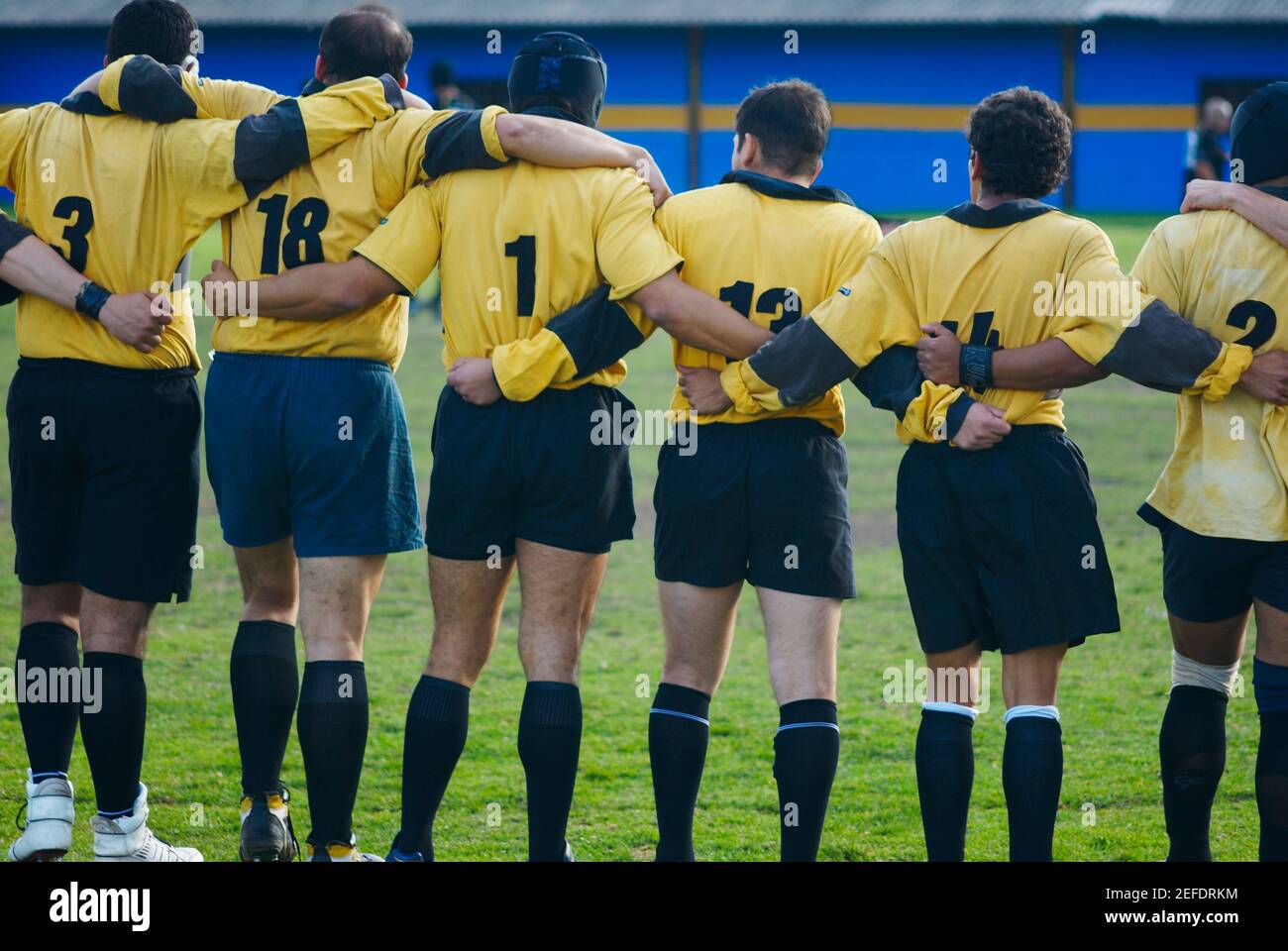 Rear view of rugby team standing with their arms around each other ...