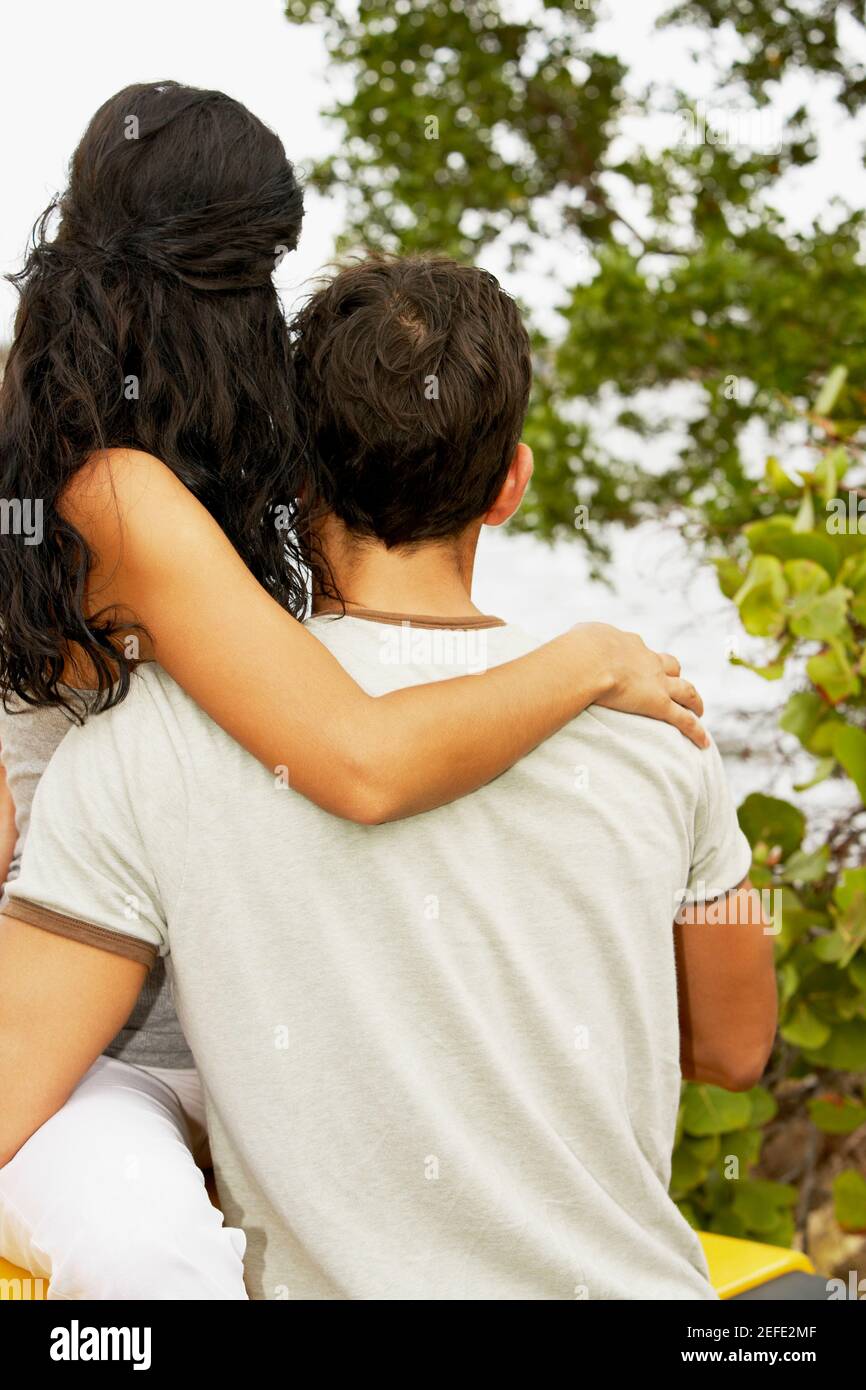 Rear view of a mid adult man and a young woman with their arms around ...