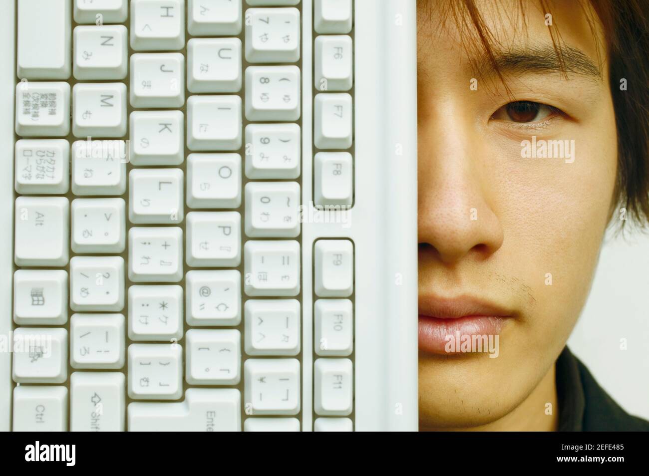 Portrait of a young man covering his face with a computer keyboard ...