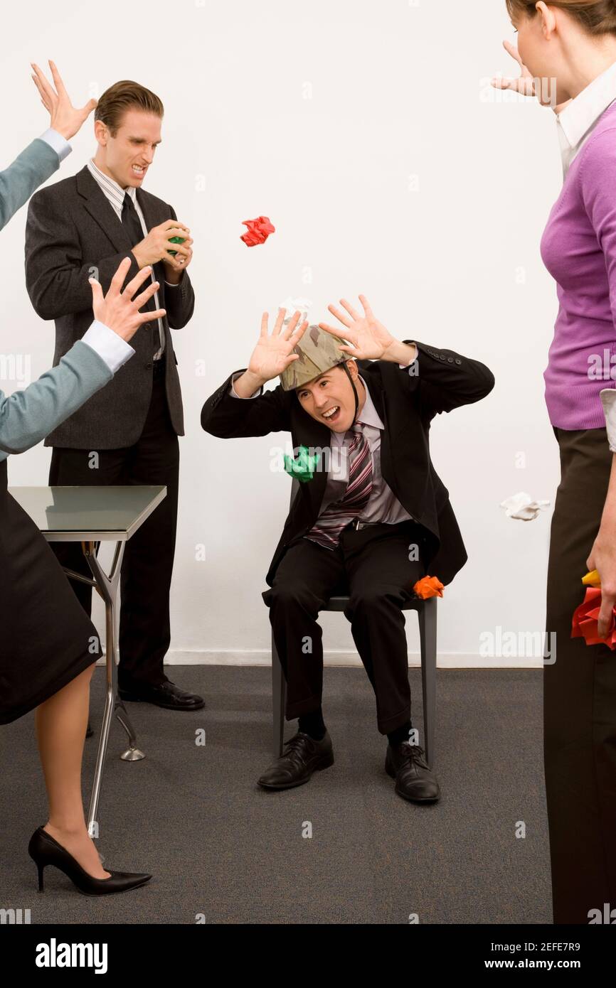 Businessman protecting himself from colleagues throwing paper balls ...