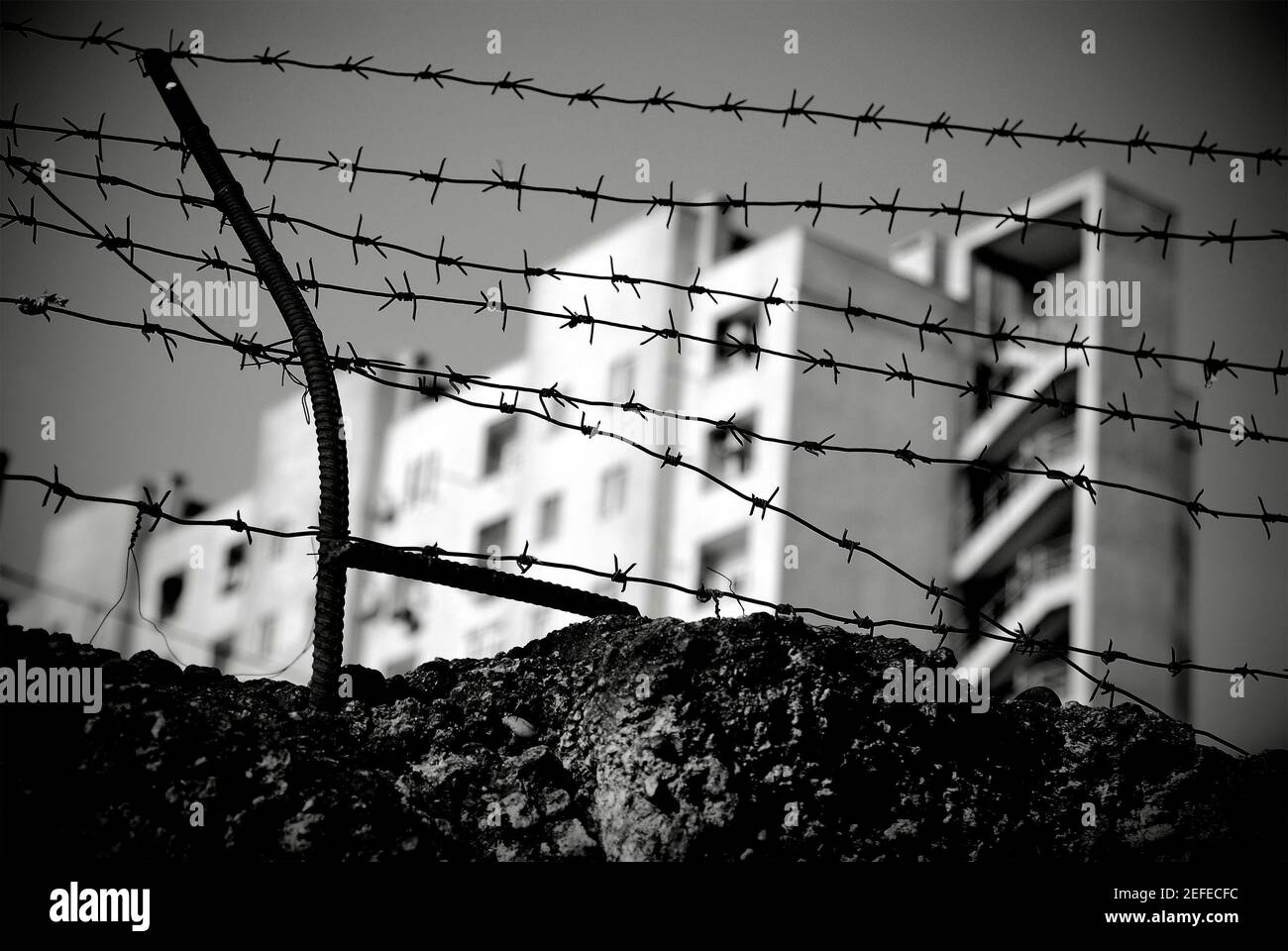 Barbed wire stretched over the wall with a multistory building seen far ...