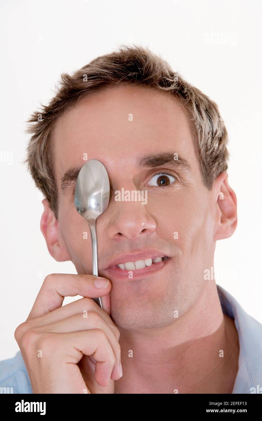 Portrait of a mid adult man holding a spoon in front of his eye Stock ...