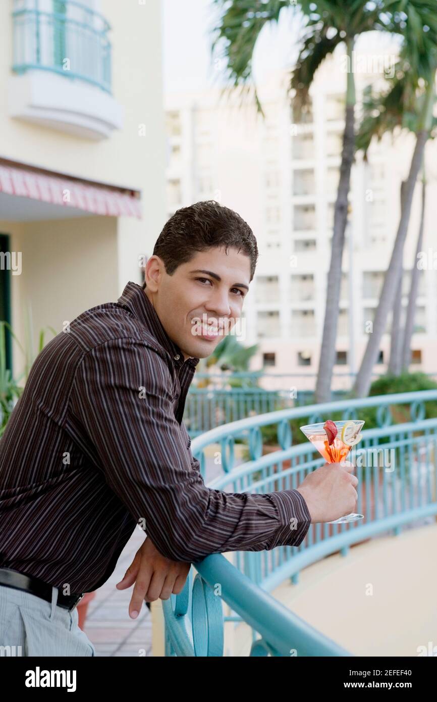 Portrait of a young man leaning against a railing and holding a ...