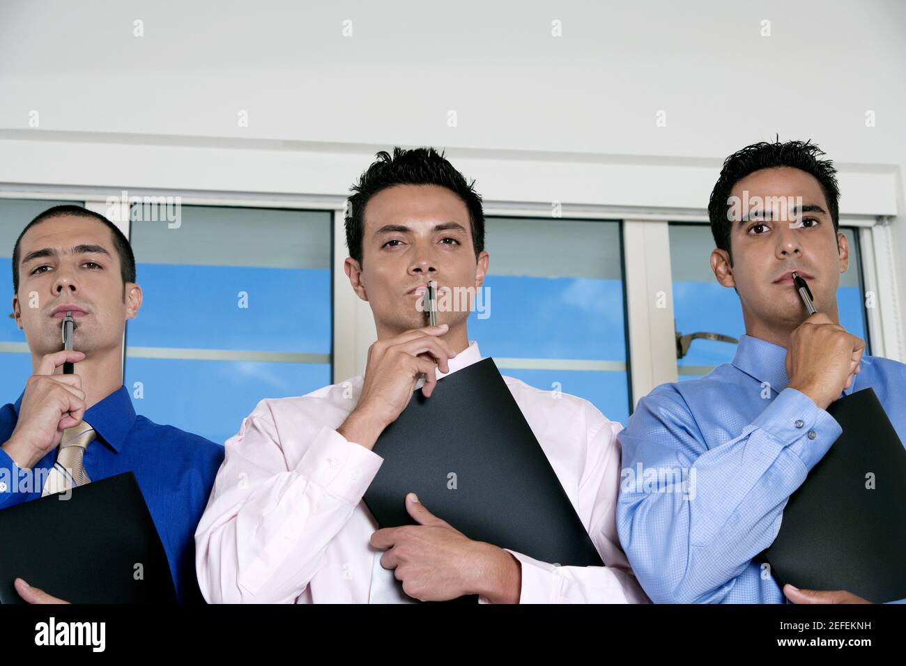 Portrait of three businessmen holding pens against their faces Stock ...