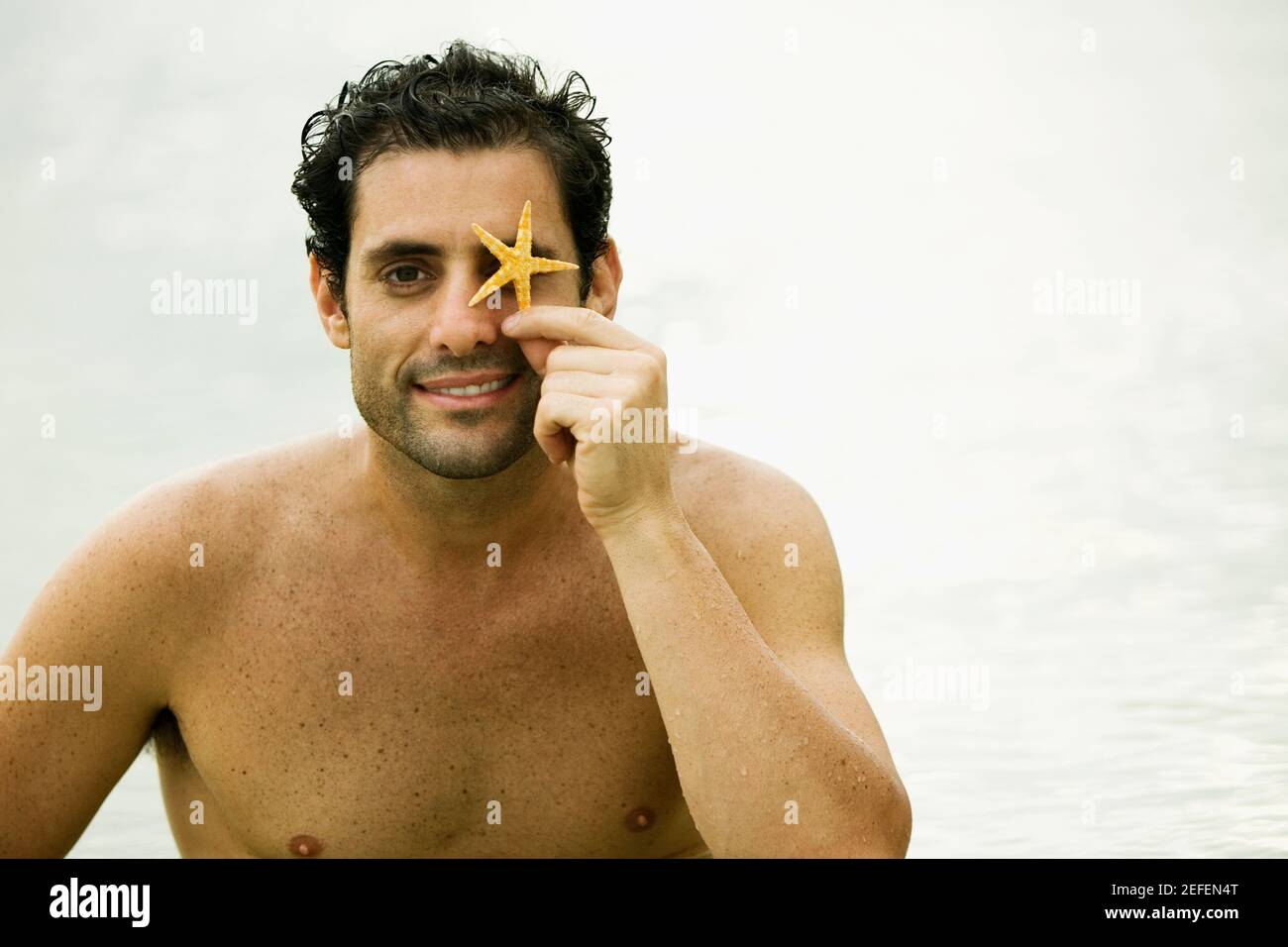 Portrait of a mid adult man holding a starfish in front of his eye ...
