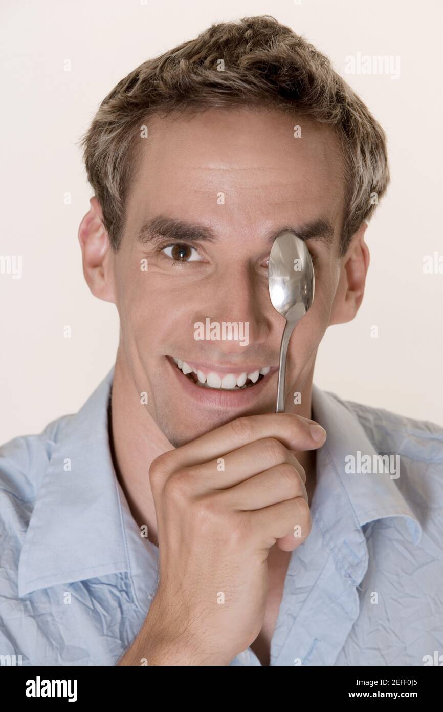 Portrait of a young man covering his eye with a spoon Stock Photo - Alamy