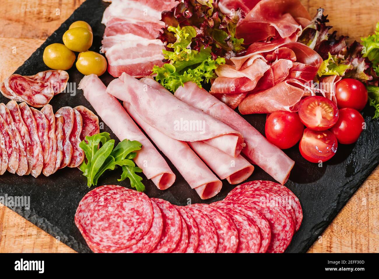 Cold cuts of different types of sausages on a black flat plate on a ...