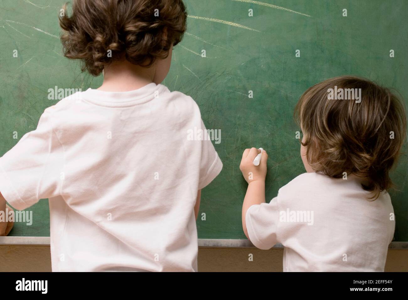 Rear view of two students drawing on a blackboard Stock Photo - Alamy