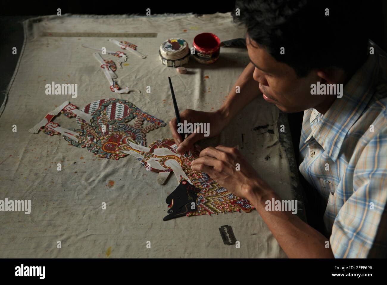Craftsman colours a wayang kulit puppet of King Kresna (Krishna) in the ...