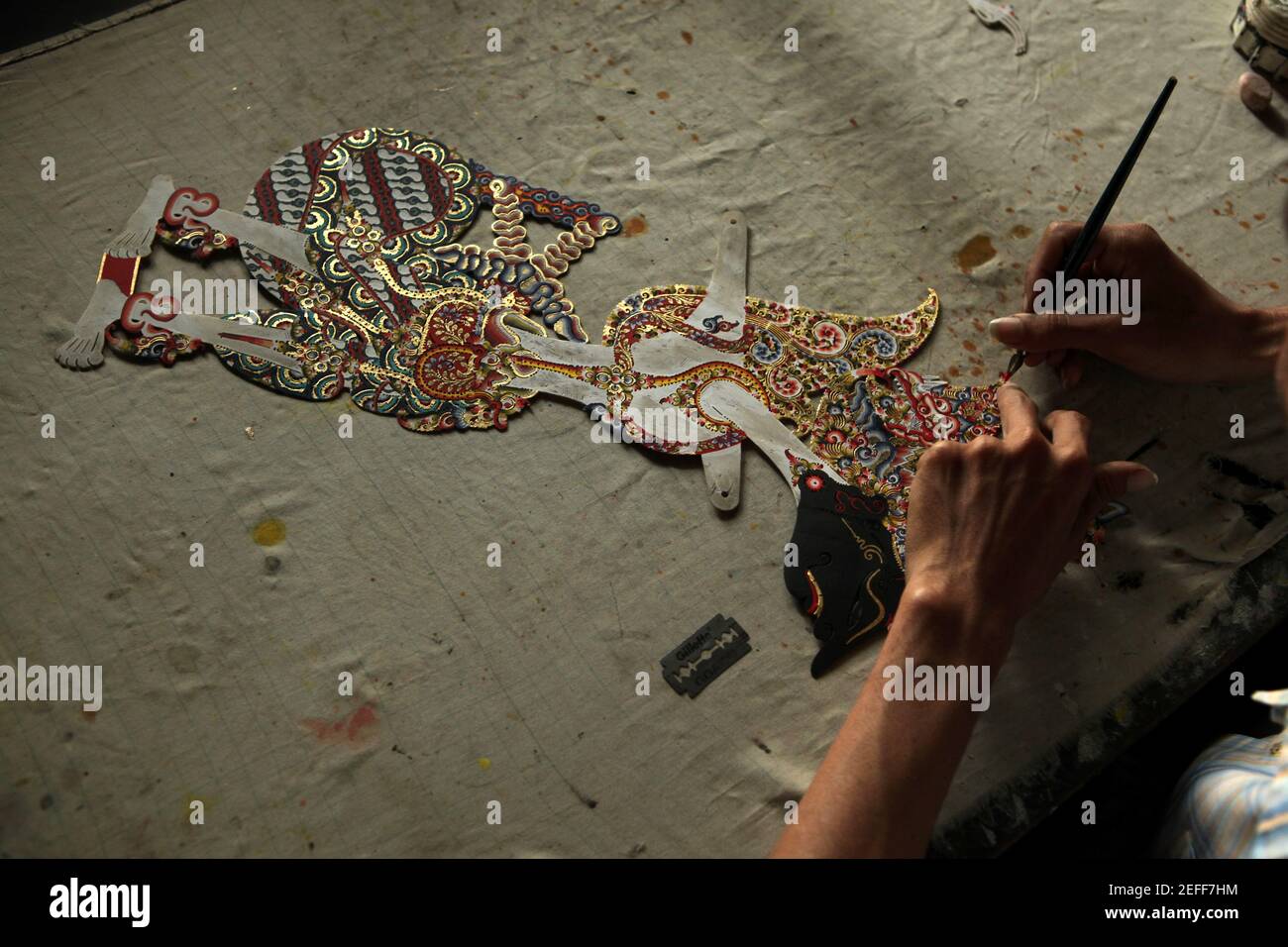 Craftsman colours a wayang kulit puppet of King Kresna (Krishna) in the ...