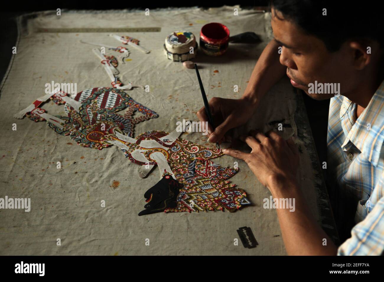 Craftsman colours a wayang kulit puppet of King Kresna (Krishna) in the ...