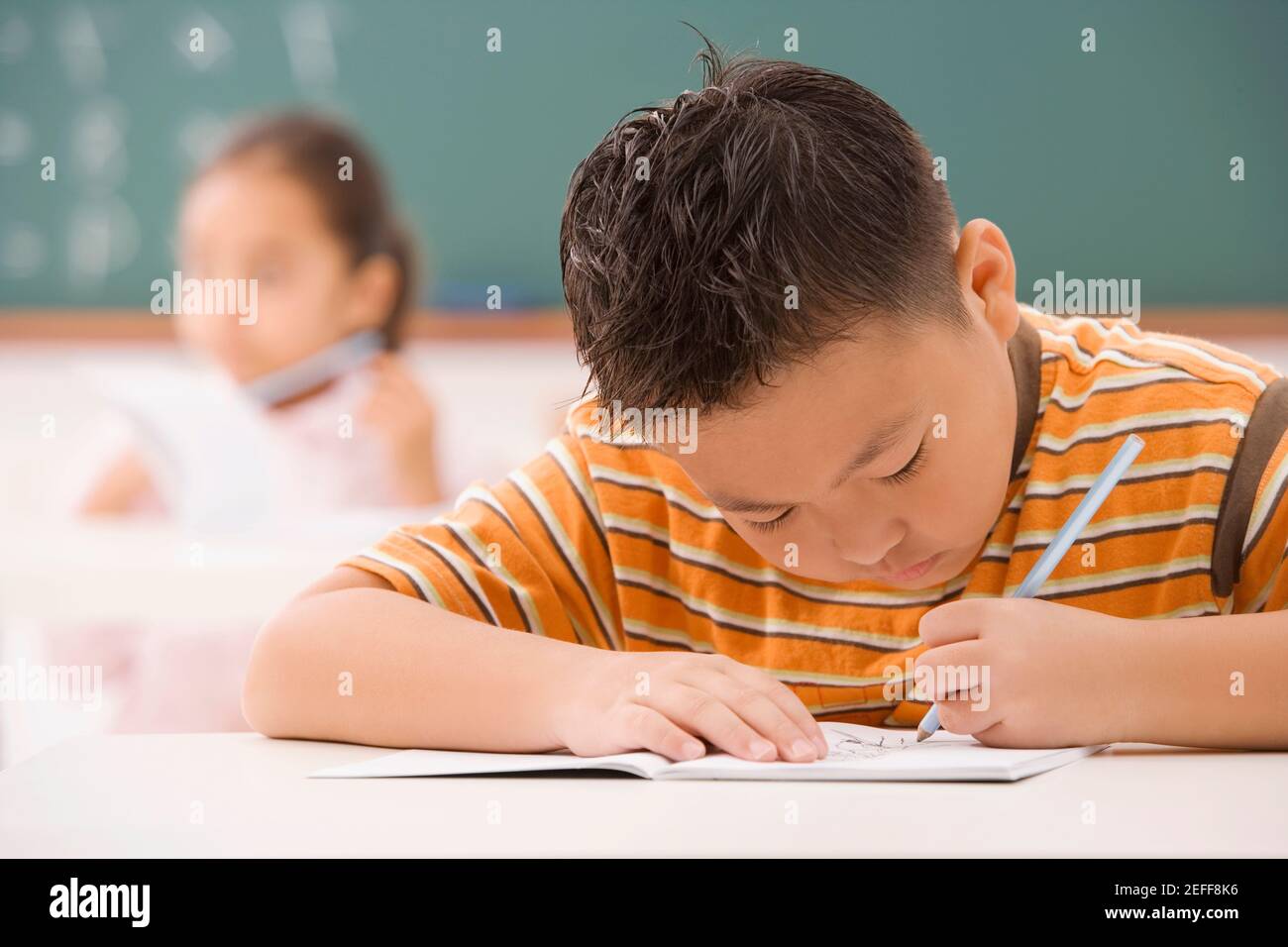 Boy writing on a notepad in a classroom Stock Photo - Alamy