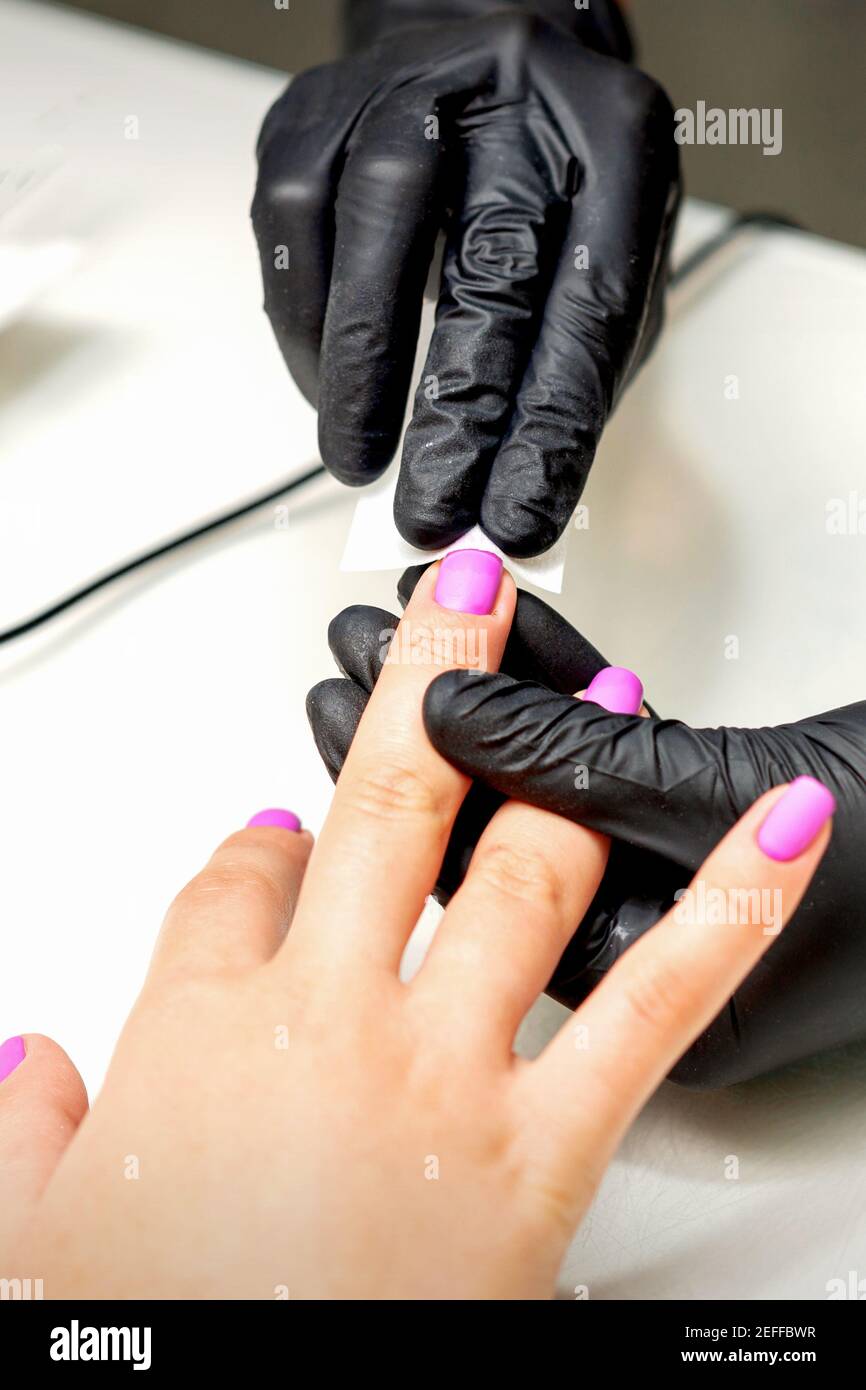 Manicurist applies a matte coating with a napkin on female pink nails ...