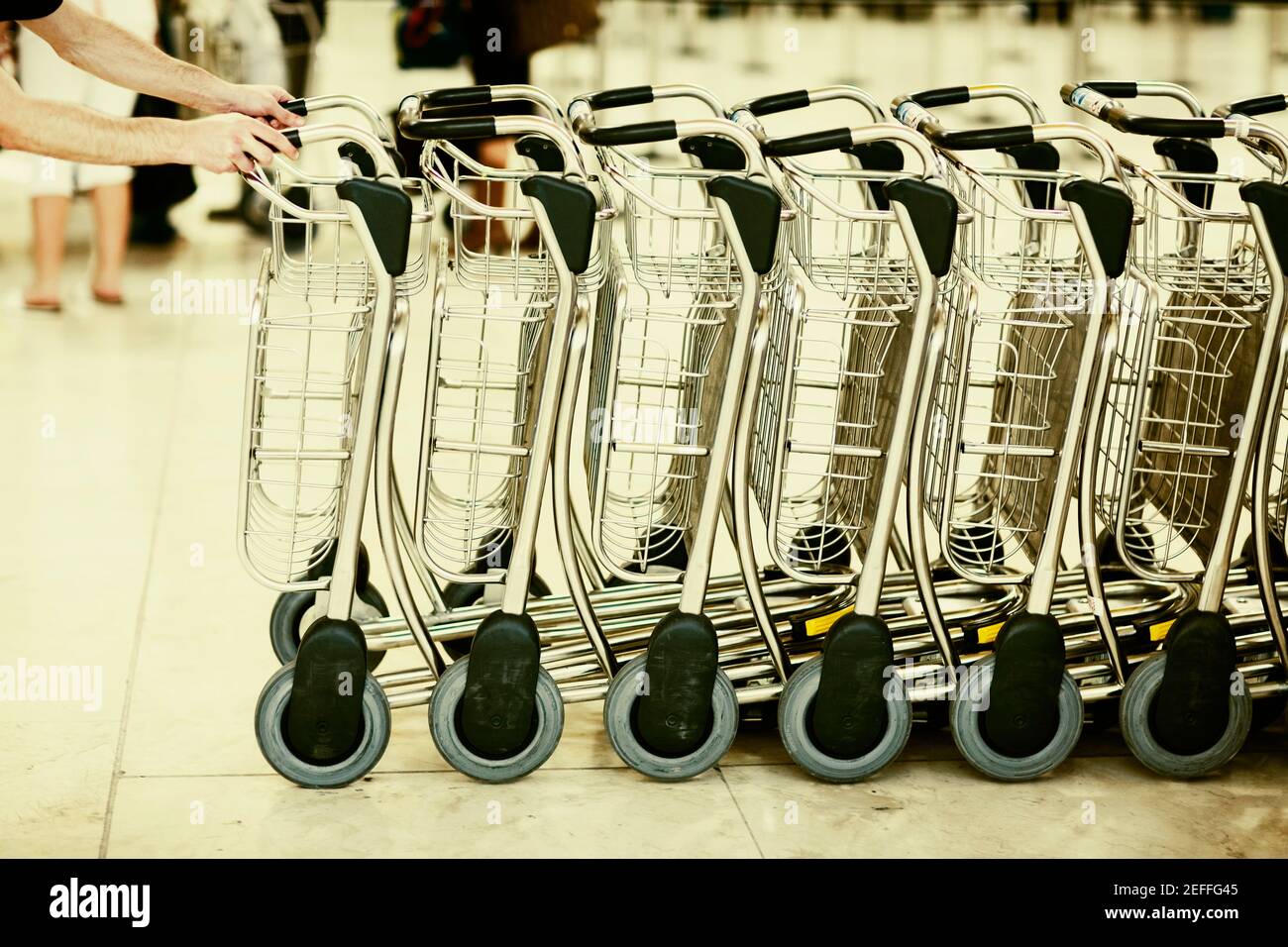 Close-up of human hands pushing a row of luggage carts at an airport ...