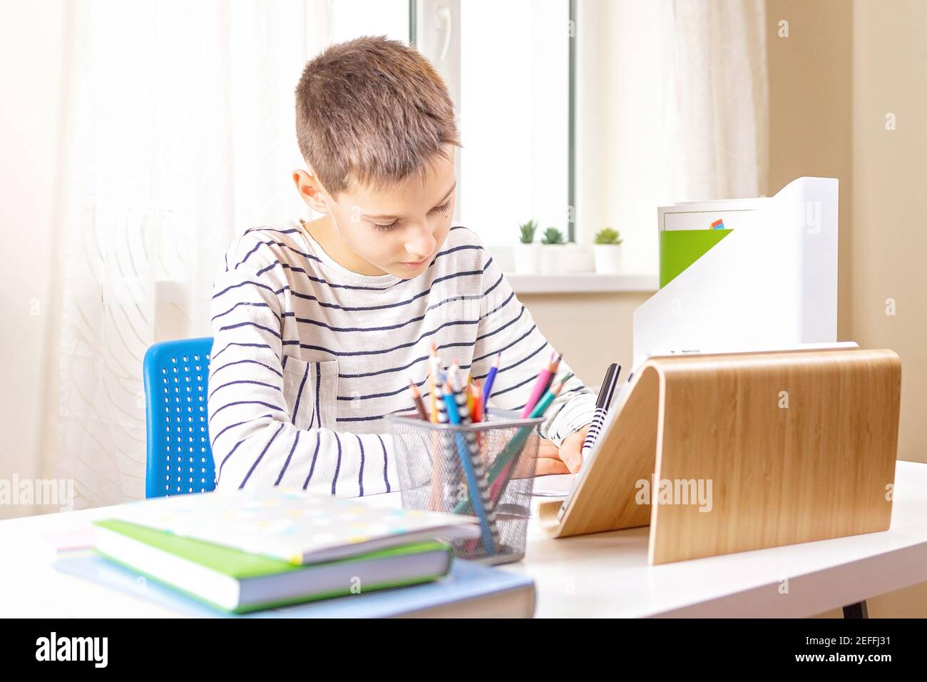 Boy with digital tablet computer writing on notebook doing homework at ...