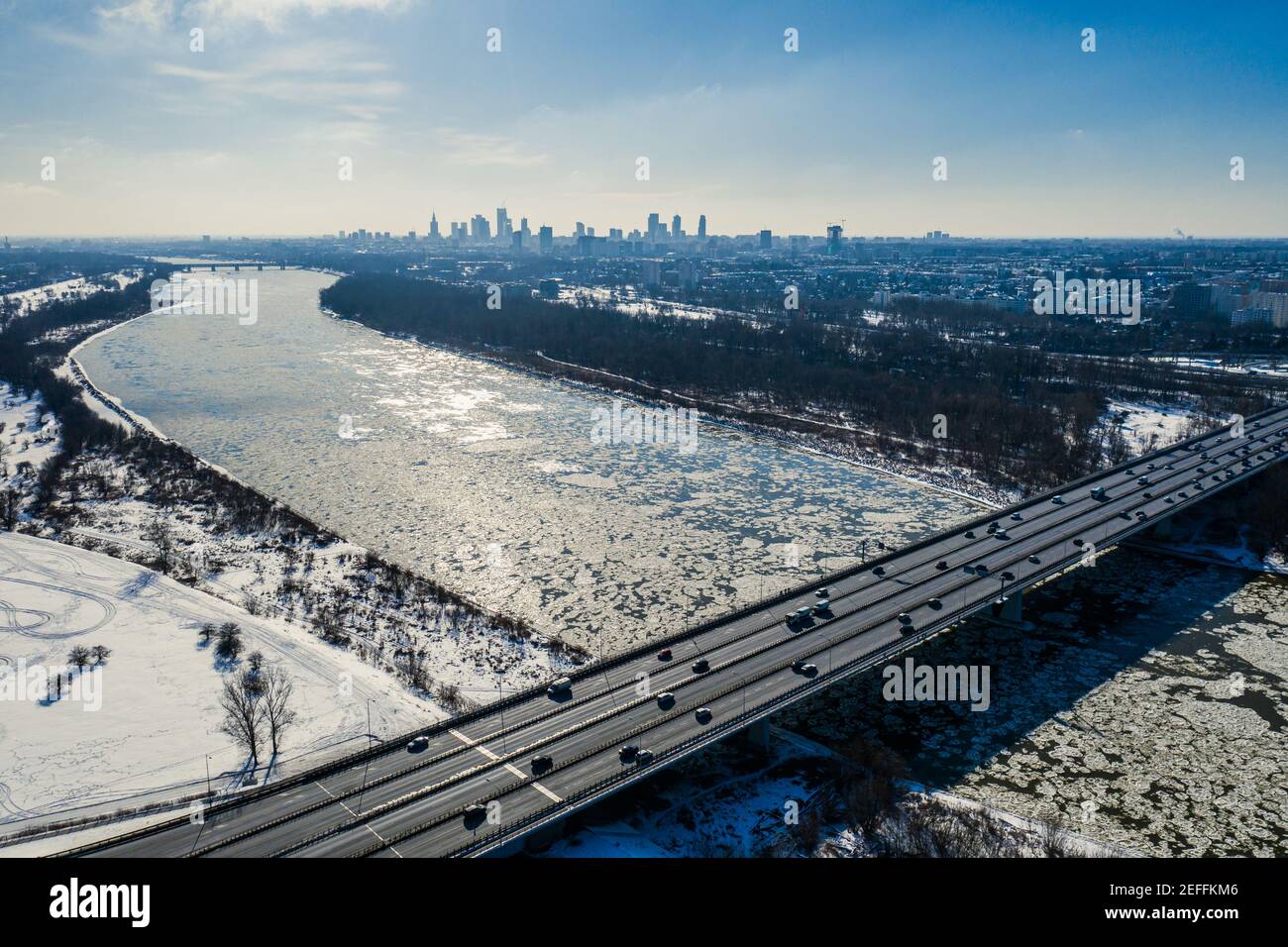 Bridge over the river covered with ice floe. Distant city center aerial ...