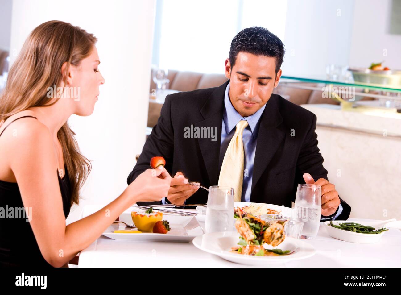 Side profile of a young woman and a mid adult man eating in a ...