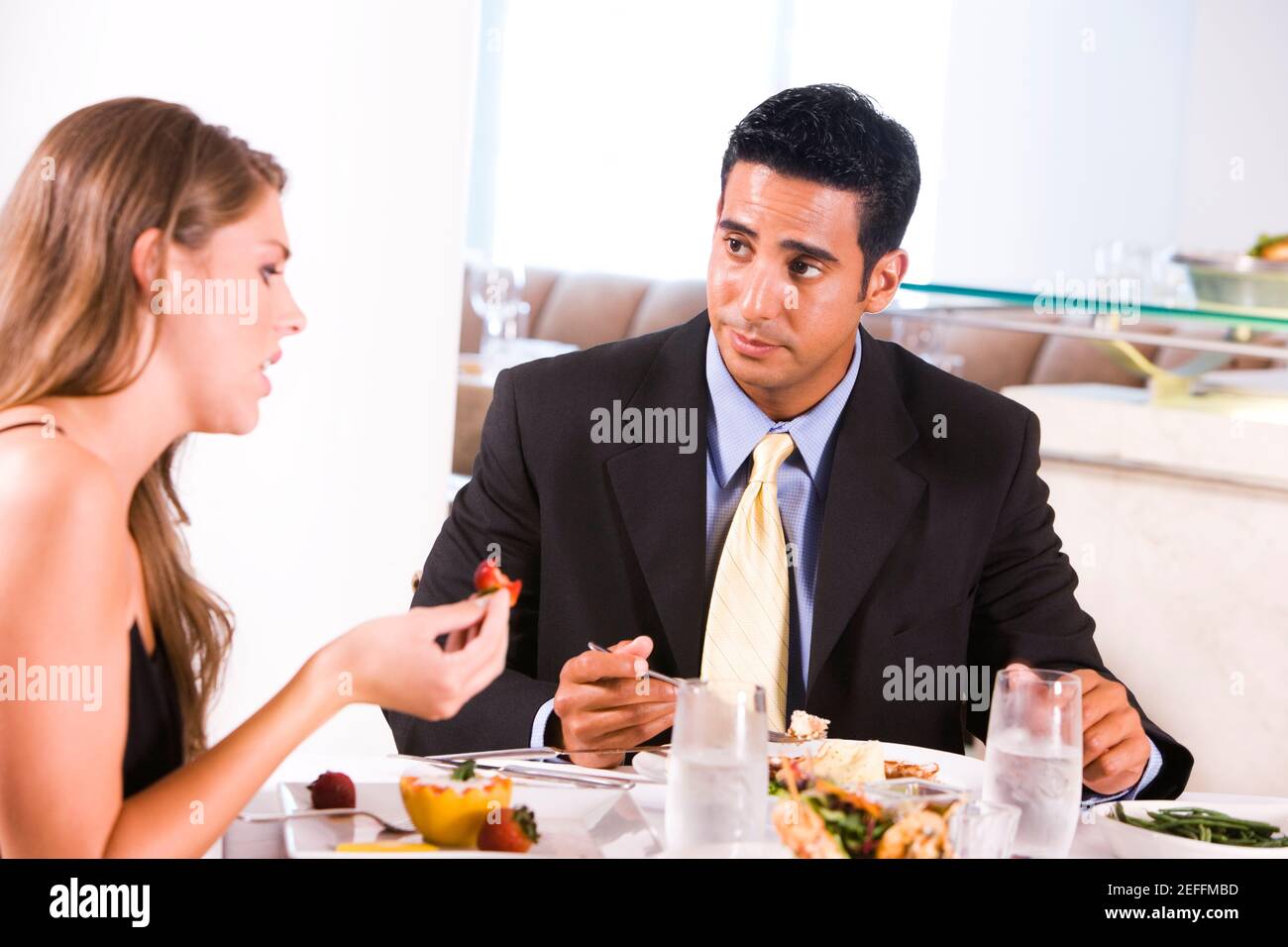 Side profile of a young woman and a mid adult man eating in a ...