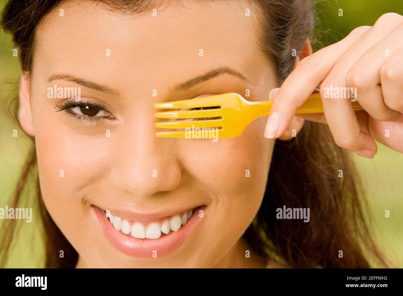 Portrait of a teenage girl holding a plastic fork in front of her eye ...