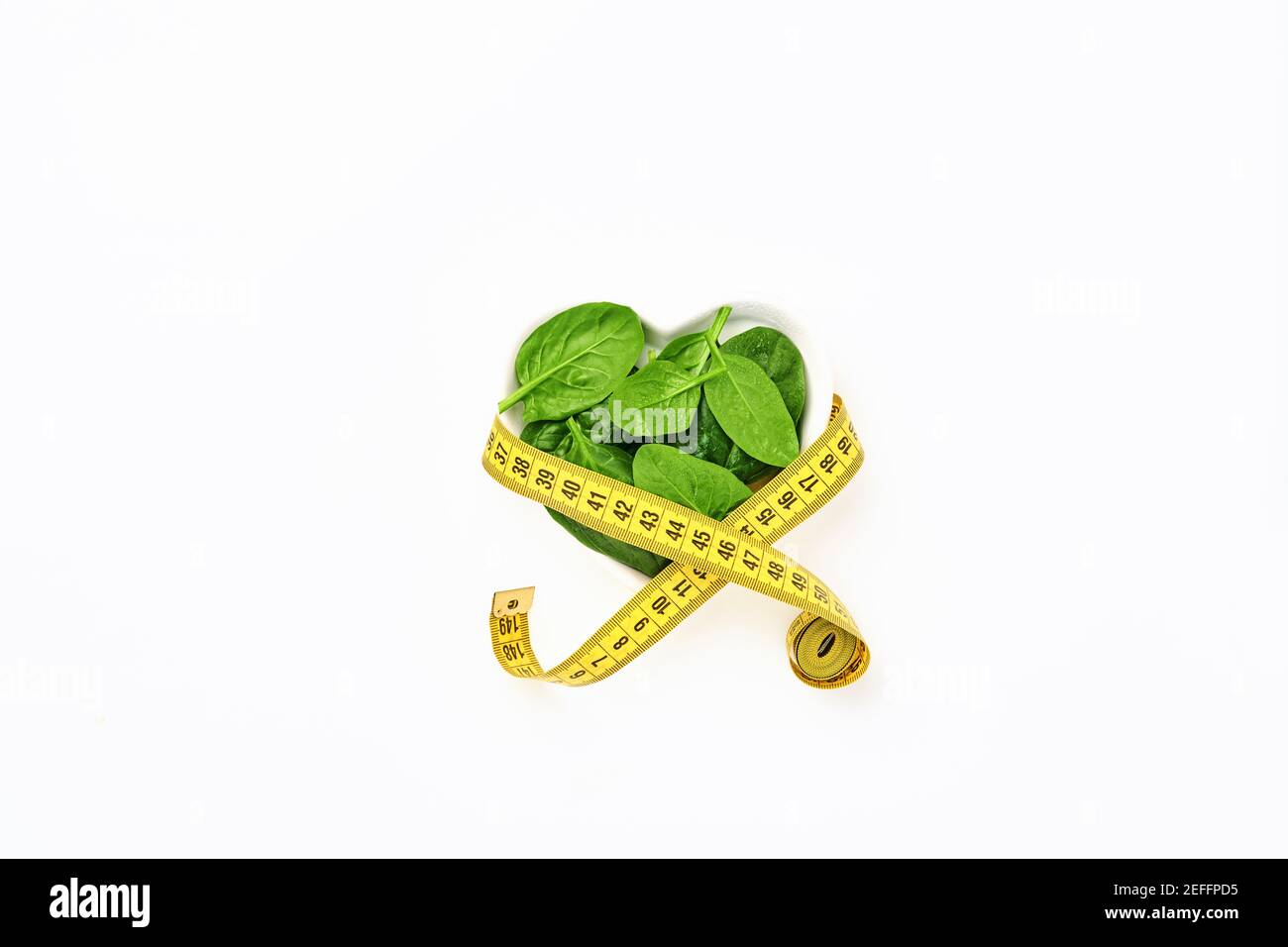 Fresh spinach leaves with measuring tape in bowl of the shape of heart ...