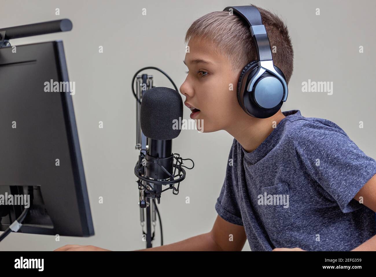 Boy talks looking to computer monitor screen. Kid wearing headphones ...