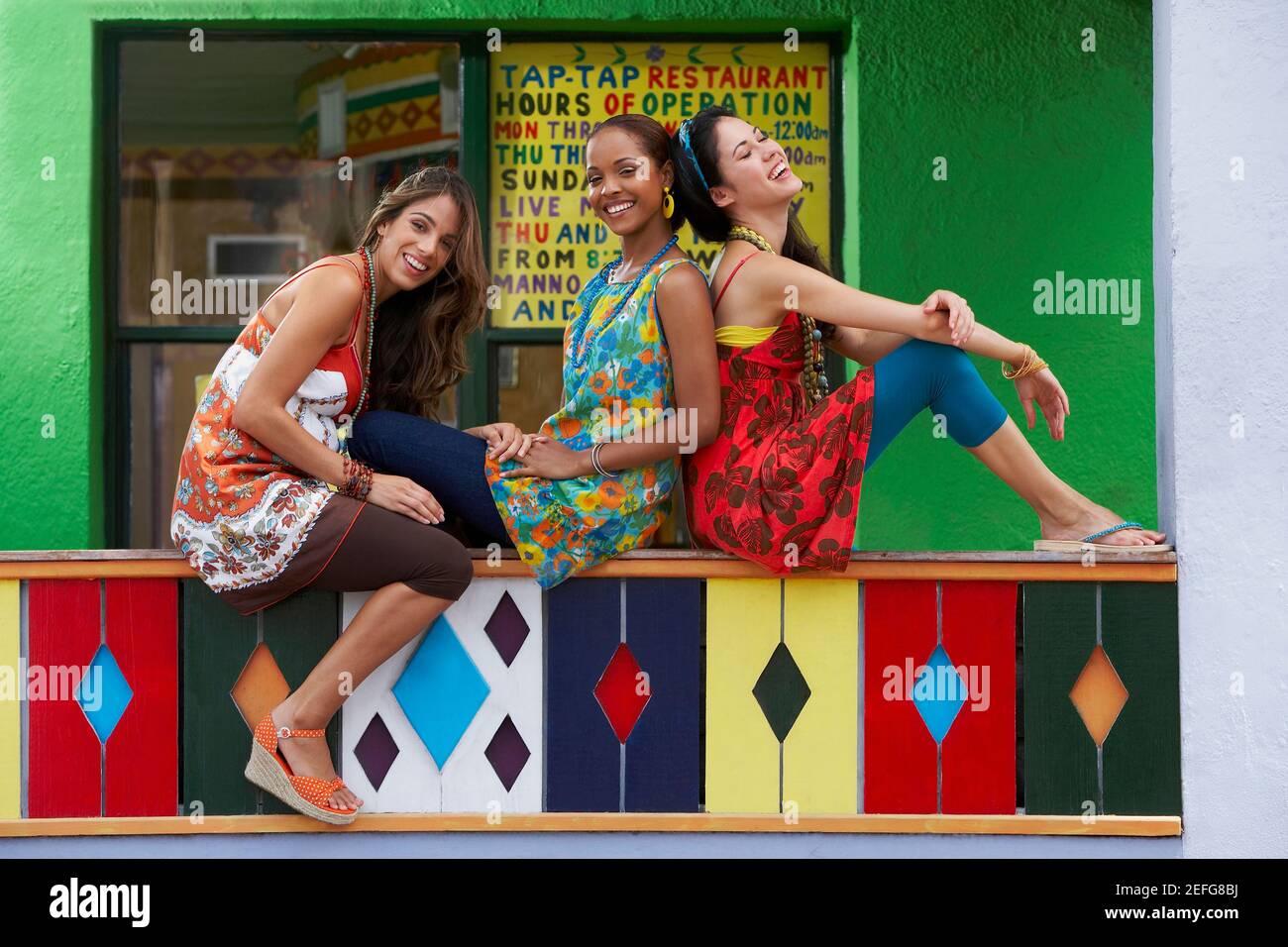 Three young women sitting on a railing and smiling Stock Photo - Alamy