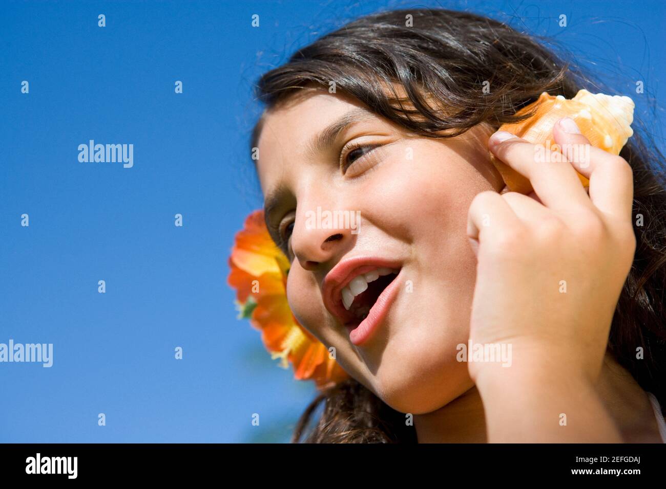 Close-up of a girl wearing flowers and listening to a conch shell Stock ...