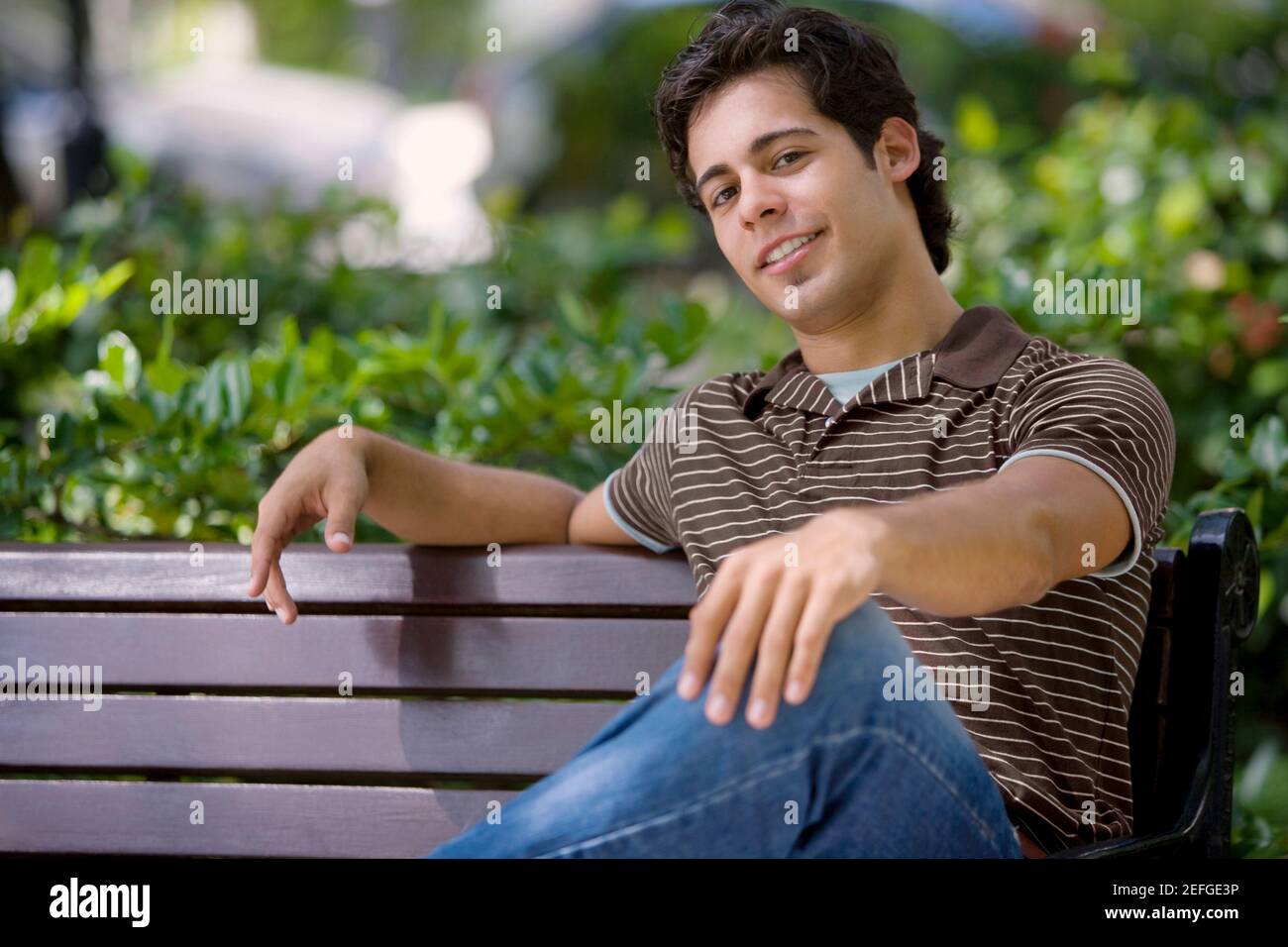 Portrait of a young man sitting on a bench with his hand on his knee ...