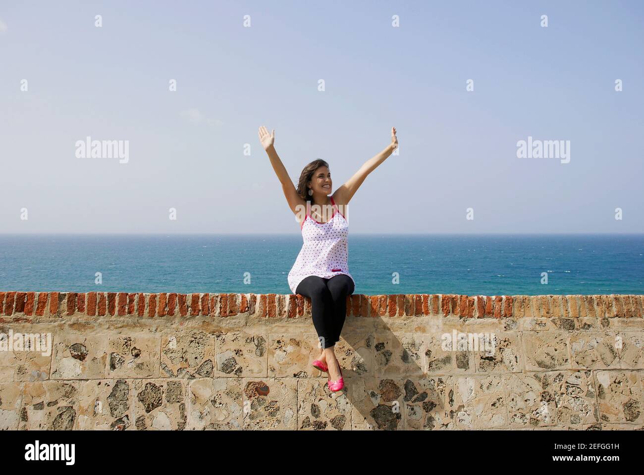 Young woman sitting on the ledge with her arms raised and smiling Stock ...