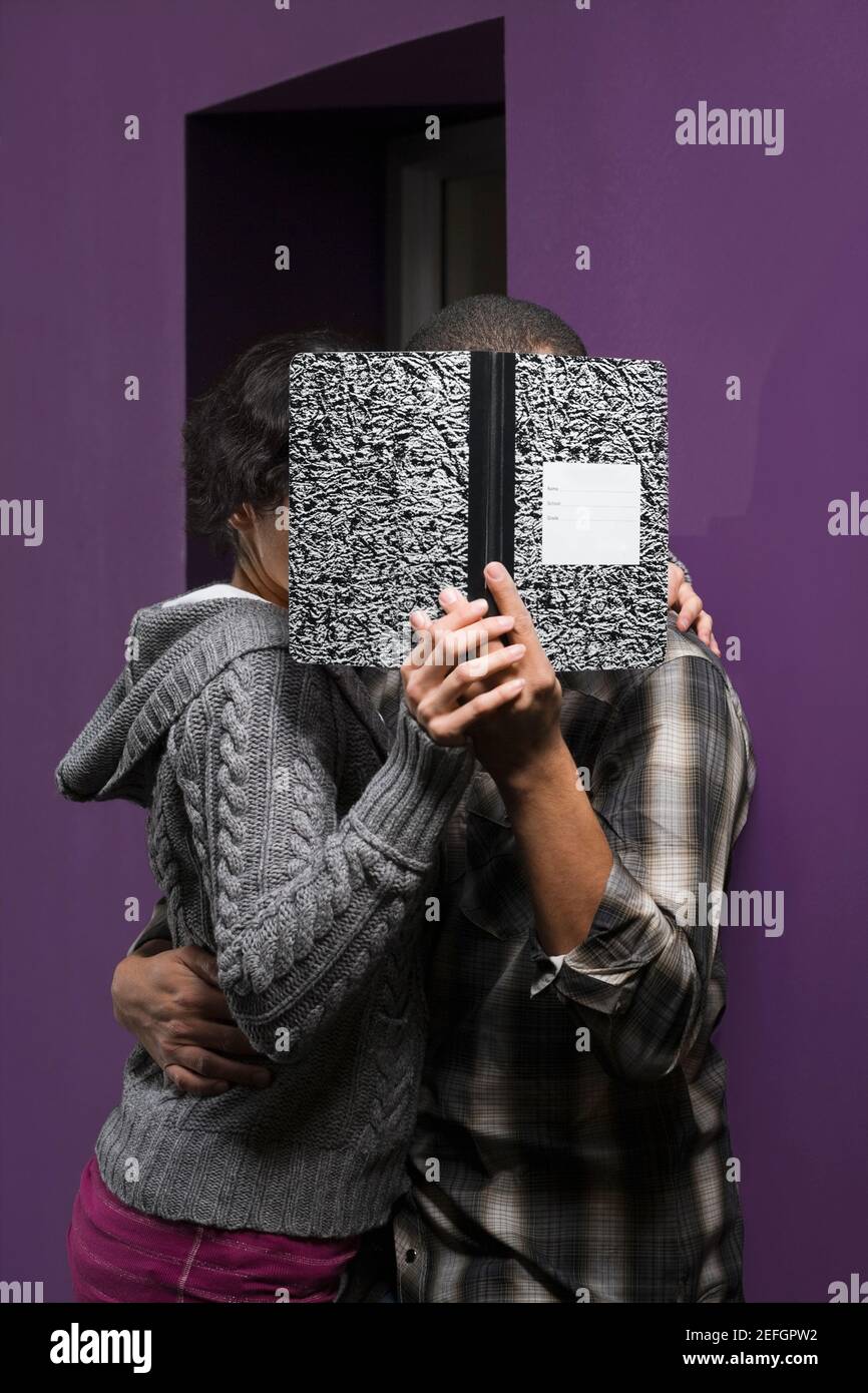 Young couple hiding their faces with a book Stock Photo - Alamy