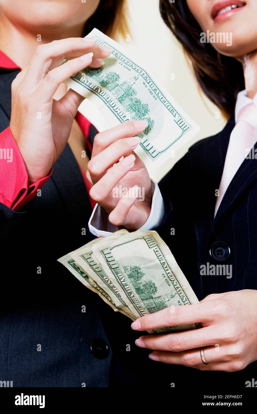 Mid section view of a businesswoman giving one hundred dollar bill to ...