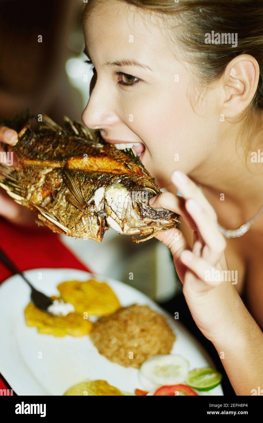 Close up of a young woman eating a grilled fish Stock Photo - Alamy