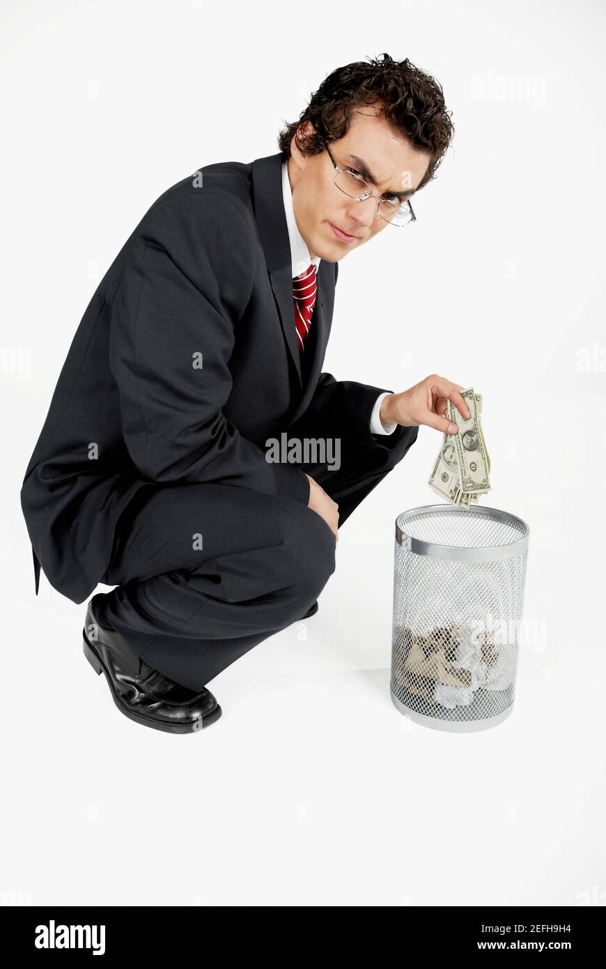 Portrait of a businessman throwing paper currency into a wastepaper ...
