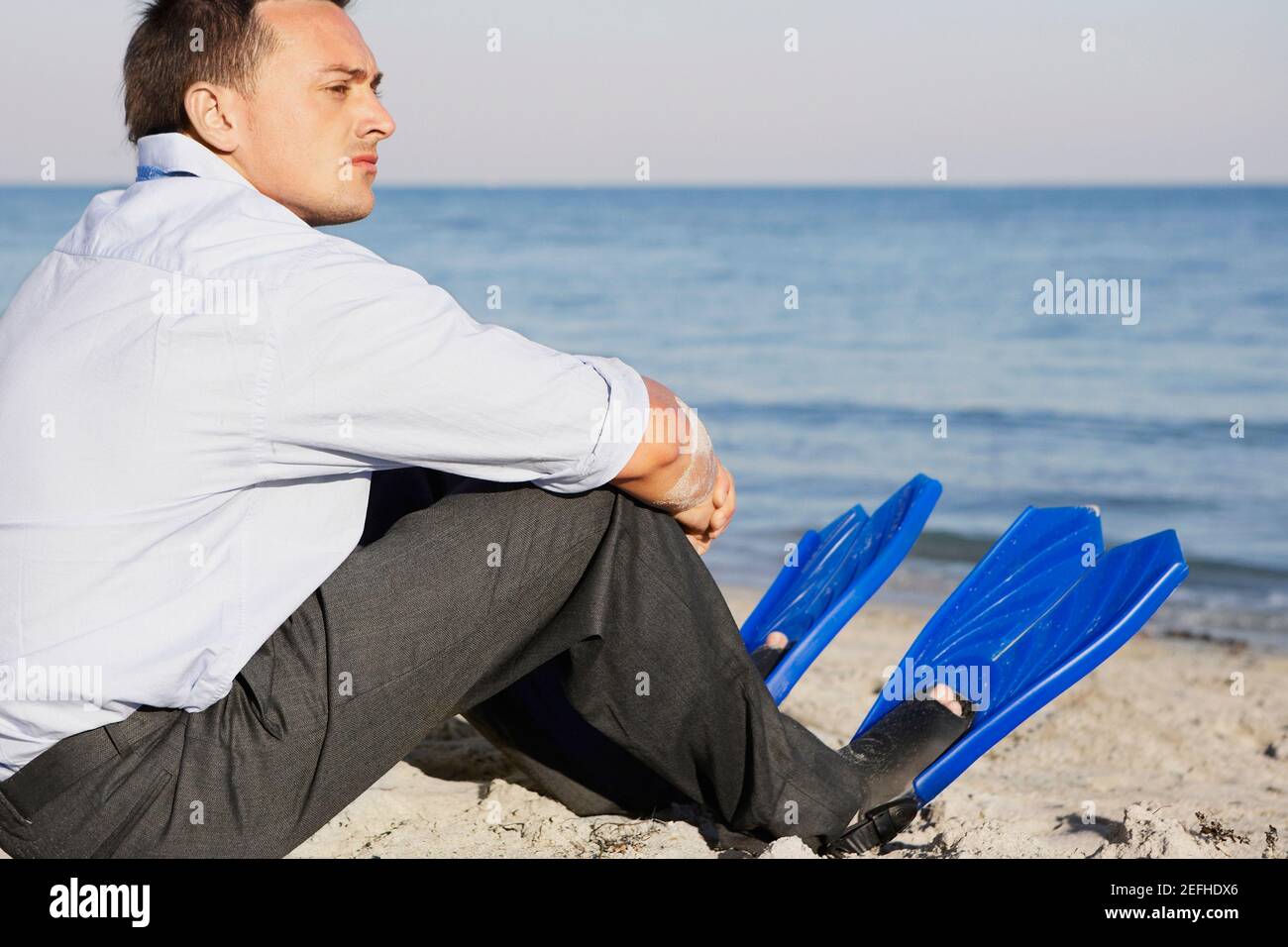 Side profile of a young man with flippers sitting on the beach Stock ...