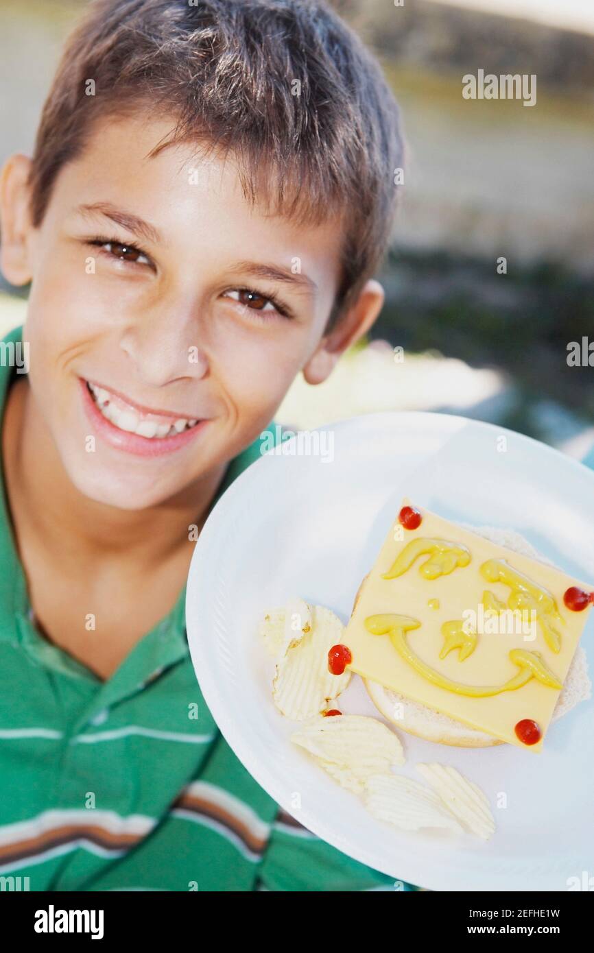 Portrait of a teenage boy showing a smiley face on a slice of cheese in ...