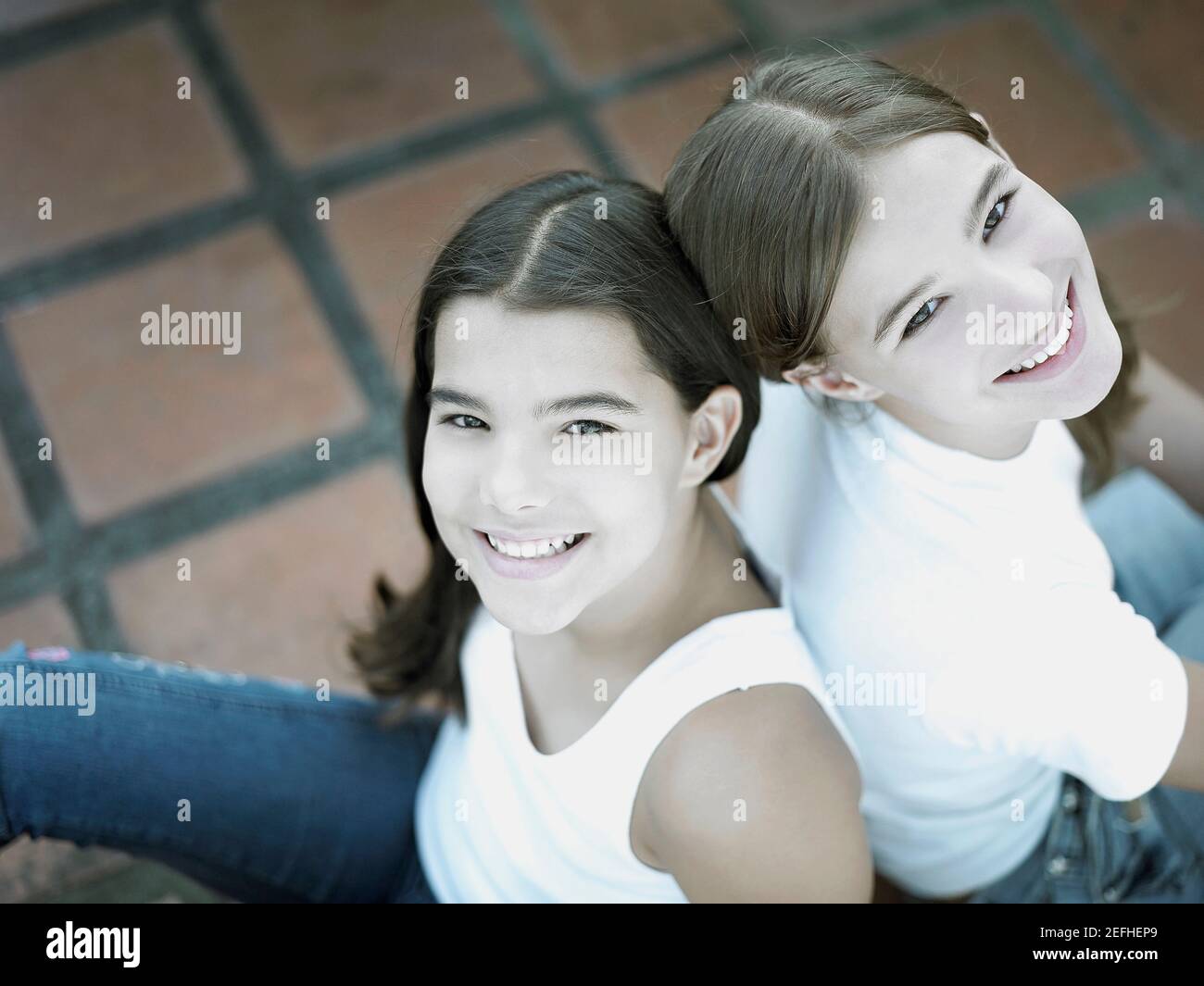 High angle view of a teenage girl and her sister sitting back to back ...